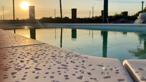 Área da piscina com deck metálico e vista desimpedida do pôr do sol ao fundo.