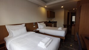 Quarto de hotel com duas camas, uma kitchenette pequena e um banheiro visível ao fundo.