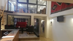 Uma sala de estar espaçosa com um sofá vermelho, cadeiras pretas e uma mesa de centro de vidro. Uma escada leva a um andar superior com uma varanda.
