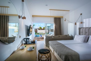 Quarto de hotel moderno com uma cama grande, um sofá, uma mesa de jantar com cafeteira e vista para a área da piscina.