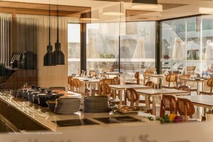 Um restaurante com mesas e cadeiras de madeira, um balcão com pratos empilhados e luminárias pendentes.