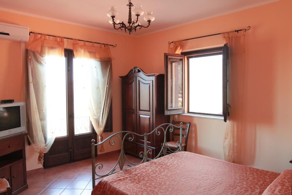 Quarto com cama, guarda-roupa, televisão e janela com cortinas.