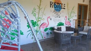 Uma cadeira suspensa com almofadas vermelhas, mobiliário de vime e um mural com flamingos e plantas.