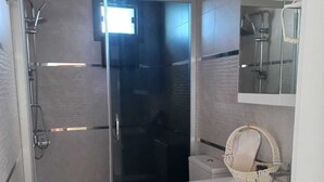 Casa de banho compacta com cabine de duche em vidro, sanita branca e lavatório com cesto.