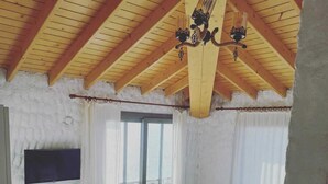 Quarto com teto de madeira, duas camas, uma televisão e uma janela grande.