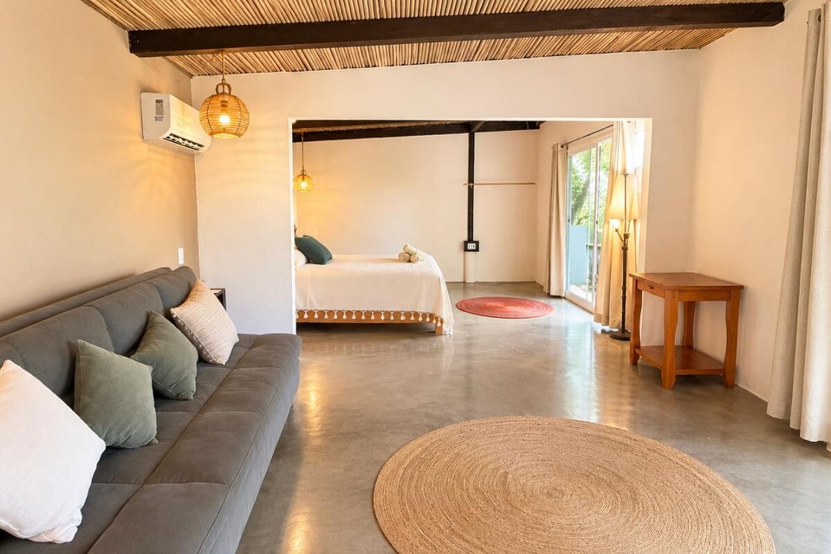 Quarto moderno com sofá, cama, tapete tecido e mesa de madeira.