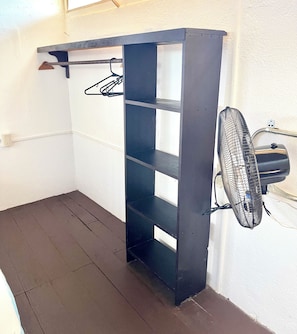 Quarto nos fundos com uma estante de madeira escura, um cabideiro e um ventilador fixado na parede.