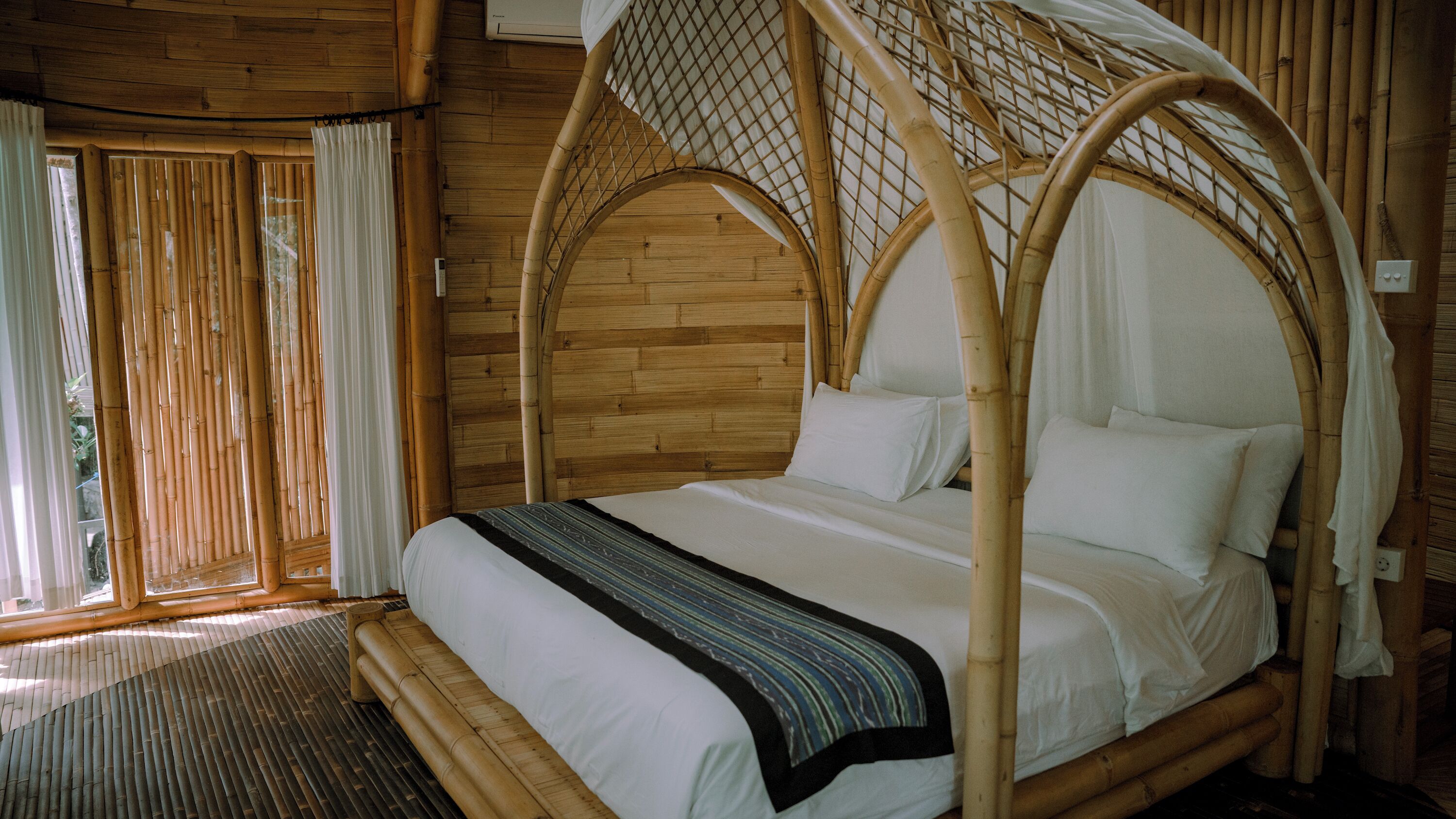 Quarto com cama de dossel, paredes de madeira e uma grande janela com cortinas.