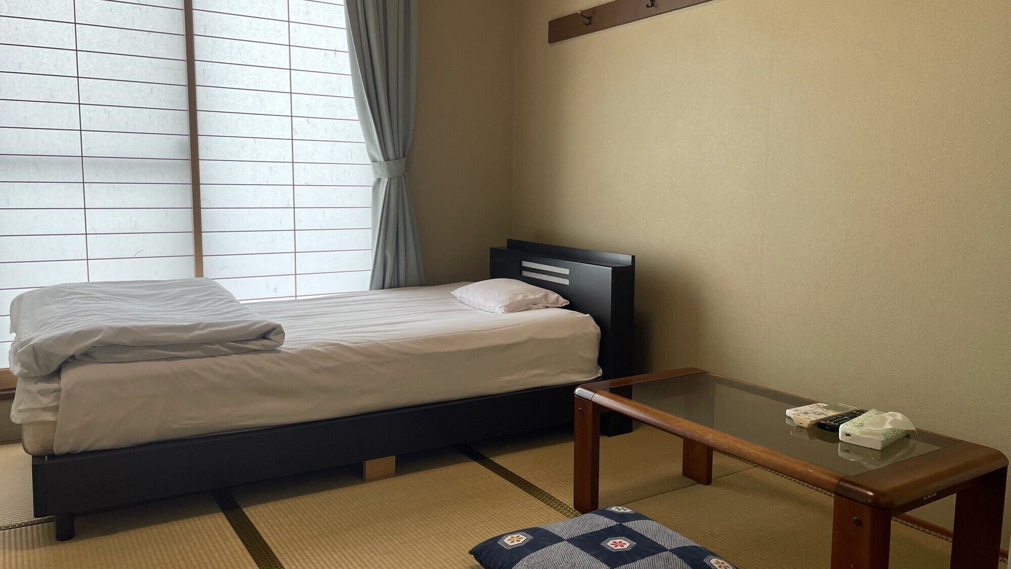 Quarto de hotel com cama, mesa pequena, travesseiro, controle remoto e caixa de lenços.