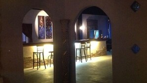 Interior com iluminação suave e portas arqueadas que dão para um bar com banquetas.