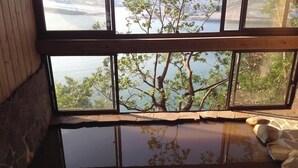 Quarto com uma grande janela com vista para a água e árvores.