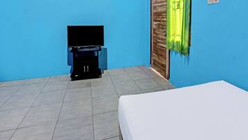 Um quarto com uma cama, uma televisão sobre um suporte e uma porta de madeira com cortina verde.
