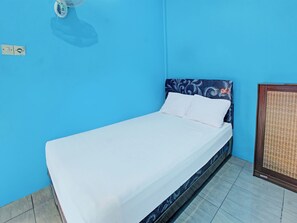 Cama de solteiro com cabeceira estampada num quarto com paredes azuis e chão de azulejos.