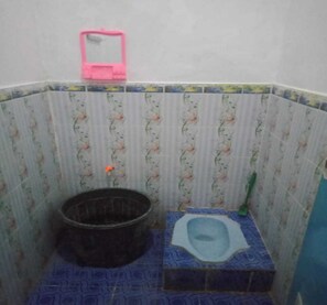 Um banheiro pequeno com vaso sanitário, um balde e um espelho rosa.