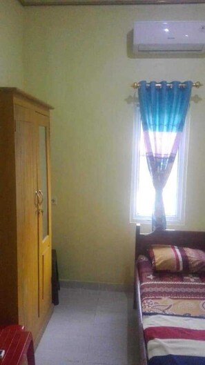 Quarto com guarda-roupa de madeira, cama com roupa de cama estampada, janela com cortinas azuis e aparelho de ar condicionado.
