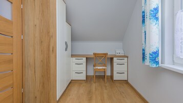 Quarto com guarda-roupa de madeira, escrivaninha com cadeira e janela com cortinas florais.