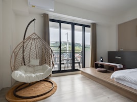 Quarto de hotel moderno com cadeira suspensa, cama, televisão e varanda com mesa e cadeiras.