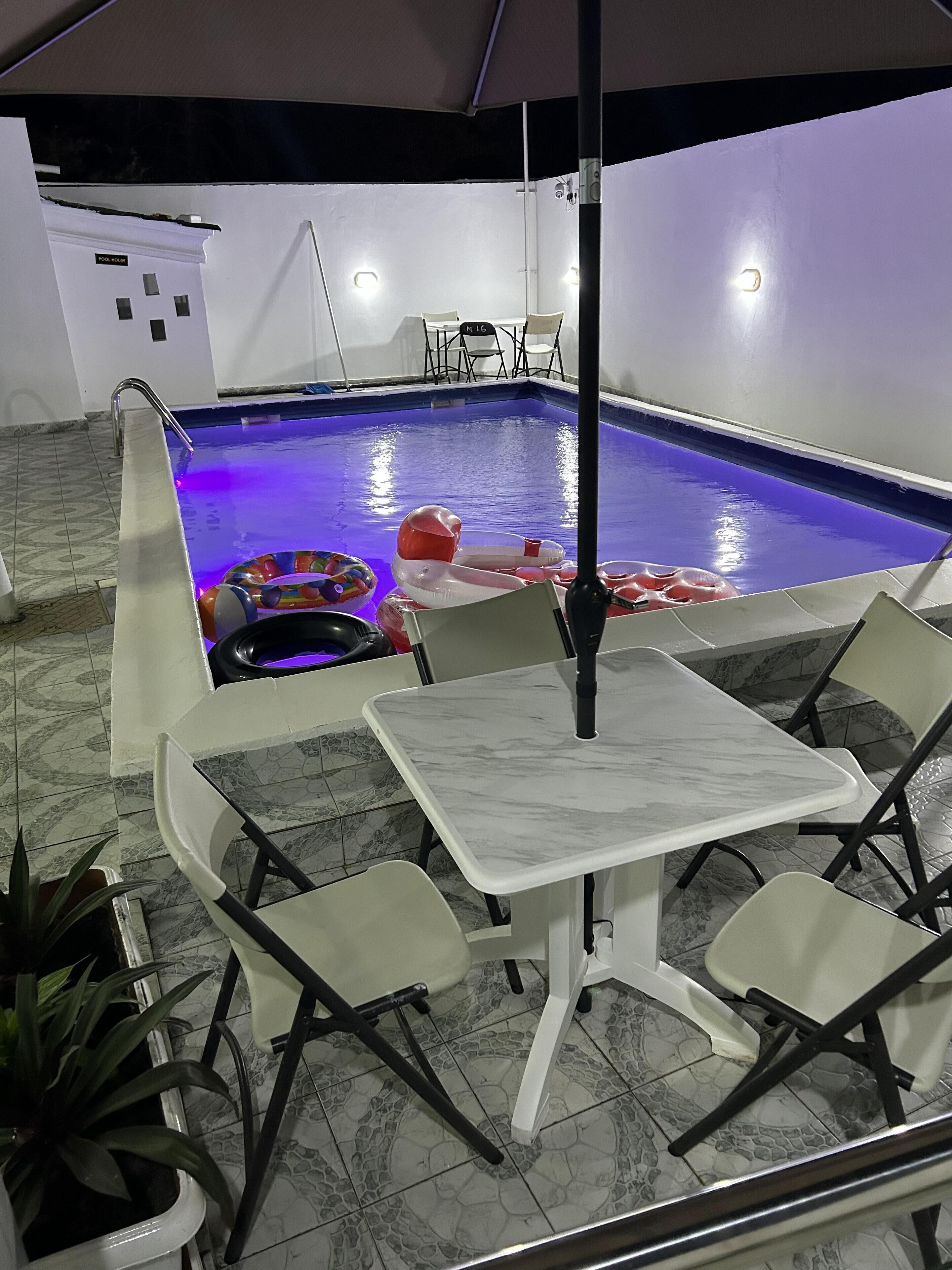 Uma área de piscina ao ar livre com mesa e cadeiras, uma espreguiçadeira à beira da piscina e um boi-de-água.