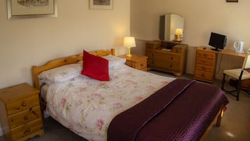 Um quarto com cama, mesas de cabeceira de madeira, cômoda, escrivaninha com computador e abajur.