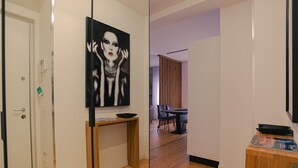Quarto moderno com piso de madeira, uma pequena mesa de madeira, um quadro na parede e uma área de refeições ao fundo.