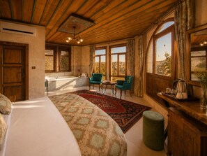 Quarto com cama, área de estar com cadeiras, janela com vista e teto de madeira.