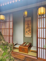 Um quarto japonês tradicional com esteiras de tatame, uma mesa de madeira baixa com chávenas verdes e um pergaminho de caligrafia na parede.