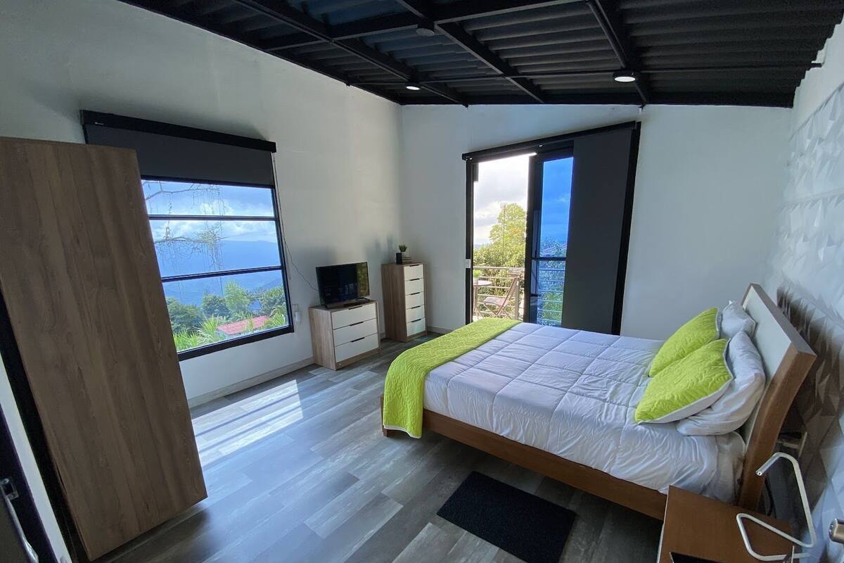 Quarto com cama, televisão, penteadeira e janela com vista.