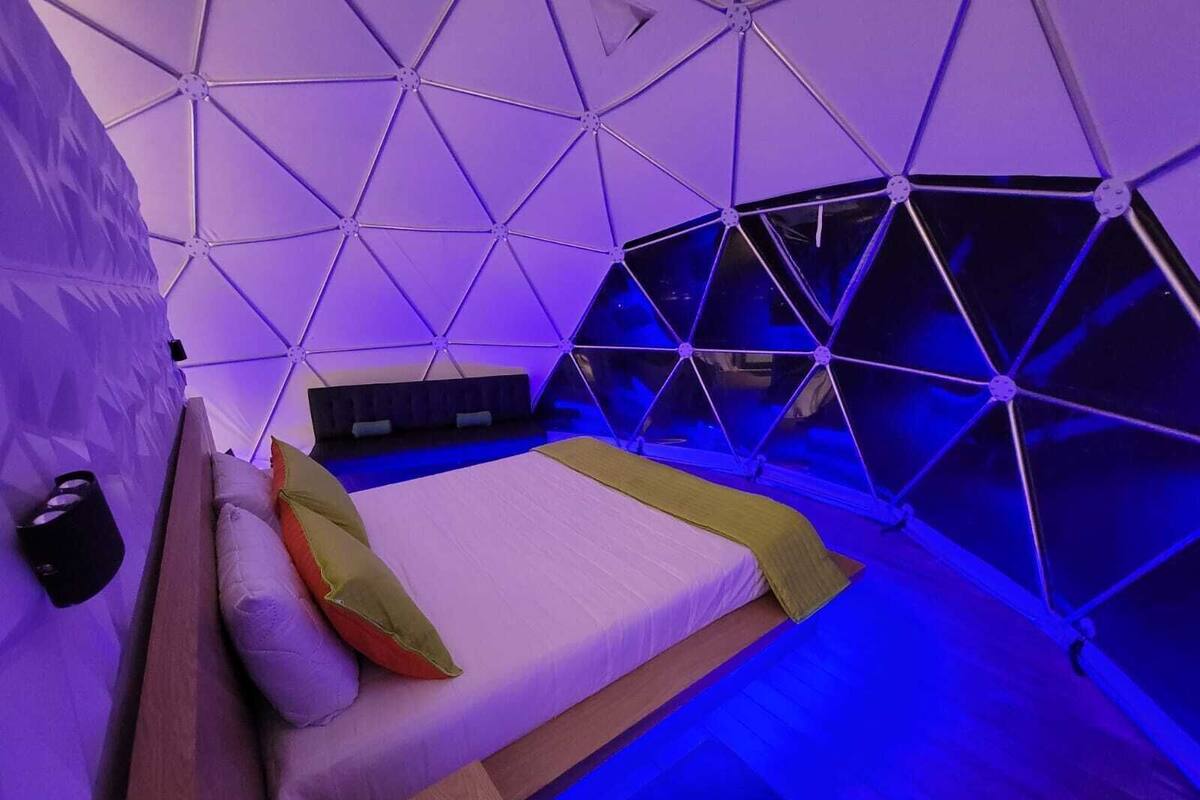 Quarto com design geométrico no teto, uma cama com almofadas e um banco.