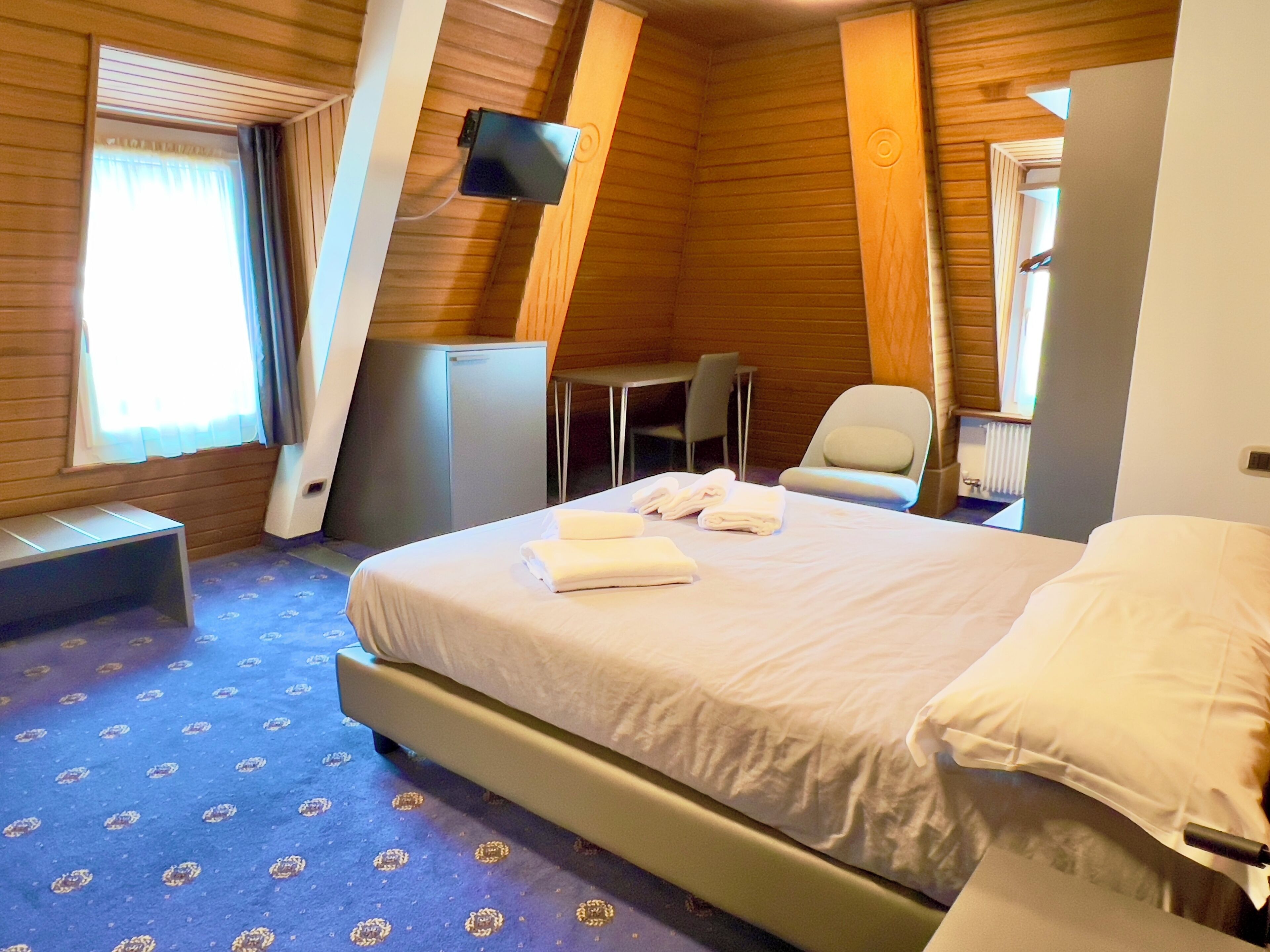 Quarto com cama, escrivaninha, cadeira, televisão e um pequeno frigorífico.