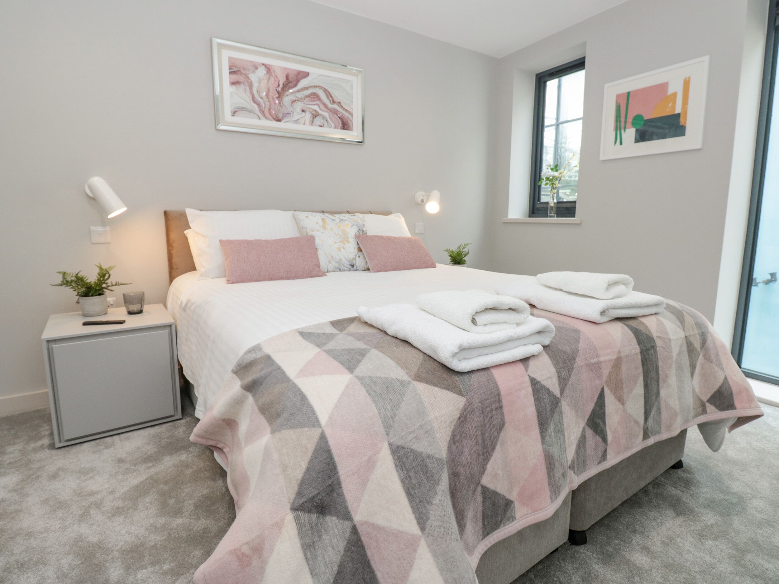 Quarto moderno com uma cama grande, mesa de cabeceira com abajur e obras de arte nas paredes.