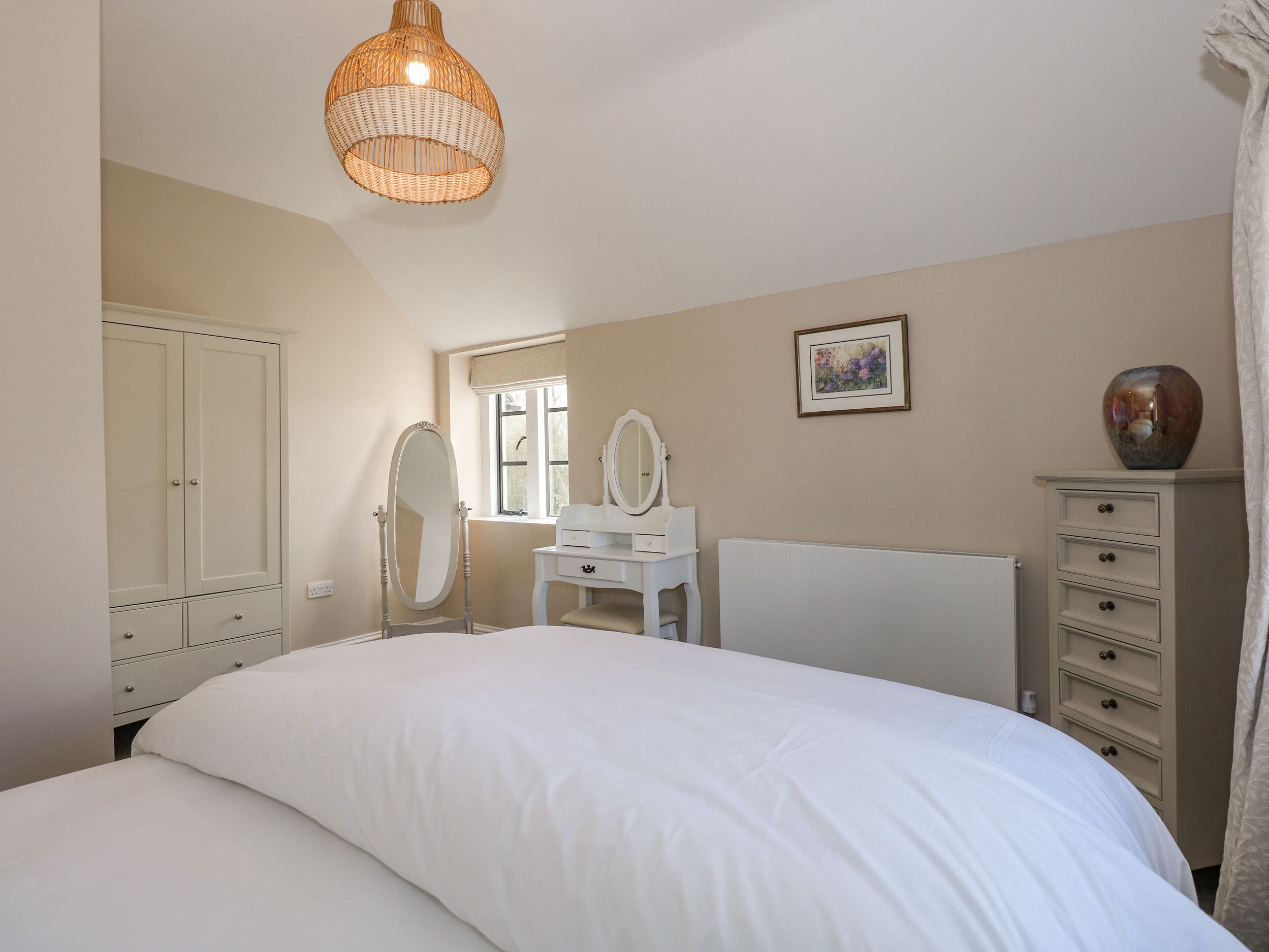 Quarto com cama, cômoda, penteadeira com espelho, guarda-roupa e luminária pendente.