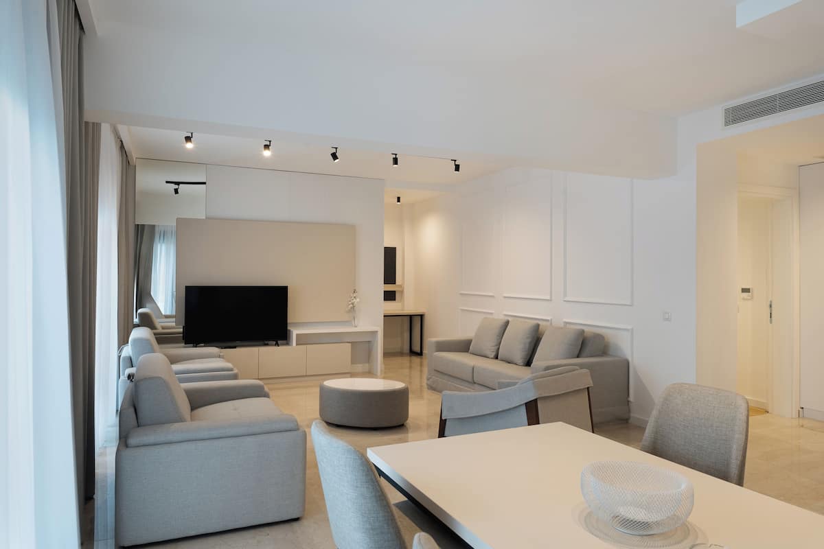 Uma sala de estar moderna com televisão de tela plana, sofás cinzas, uma mesa de jantar e iluminação embutida.