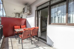 Uma varanda com mesa e cadeiras, uma divisória vermelha e uma porta de vidro deslizante que dá para uma escadaria.