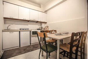 Uma cozinha compacta com armários brancos, forno embutido e um espaço de refeições com mesa e cadeiras.