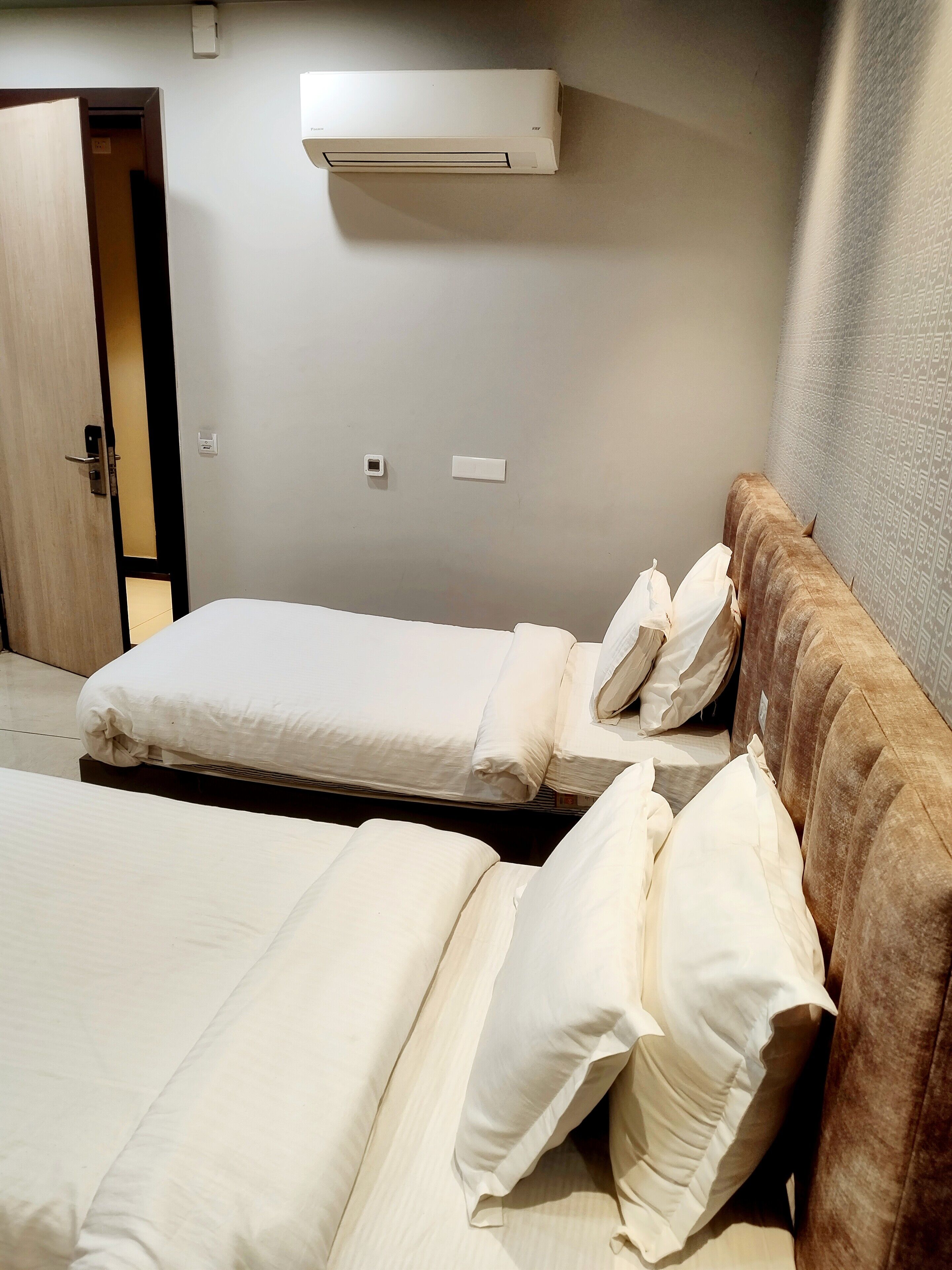 Quarto de hotel com duas camas, um guarda-roupa e ar condicionado fixado na parede.