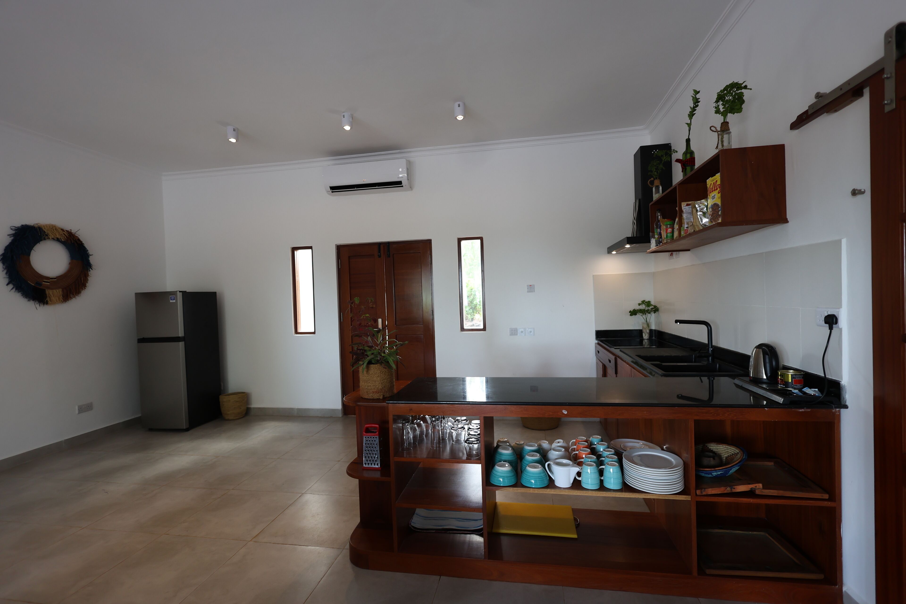 Cozinha moderna com ilha central, eletrodomésticos embutidos e prateleira de madeira sobre a pia.