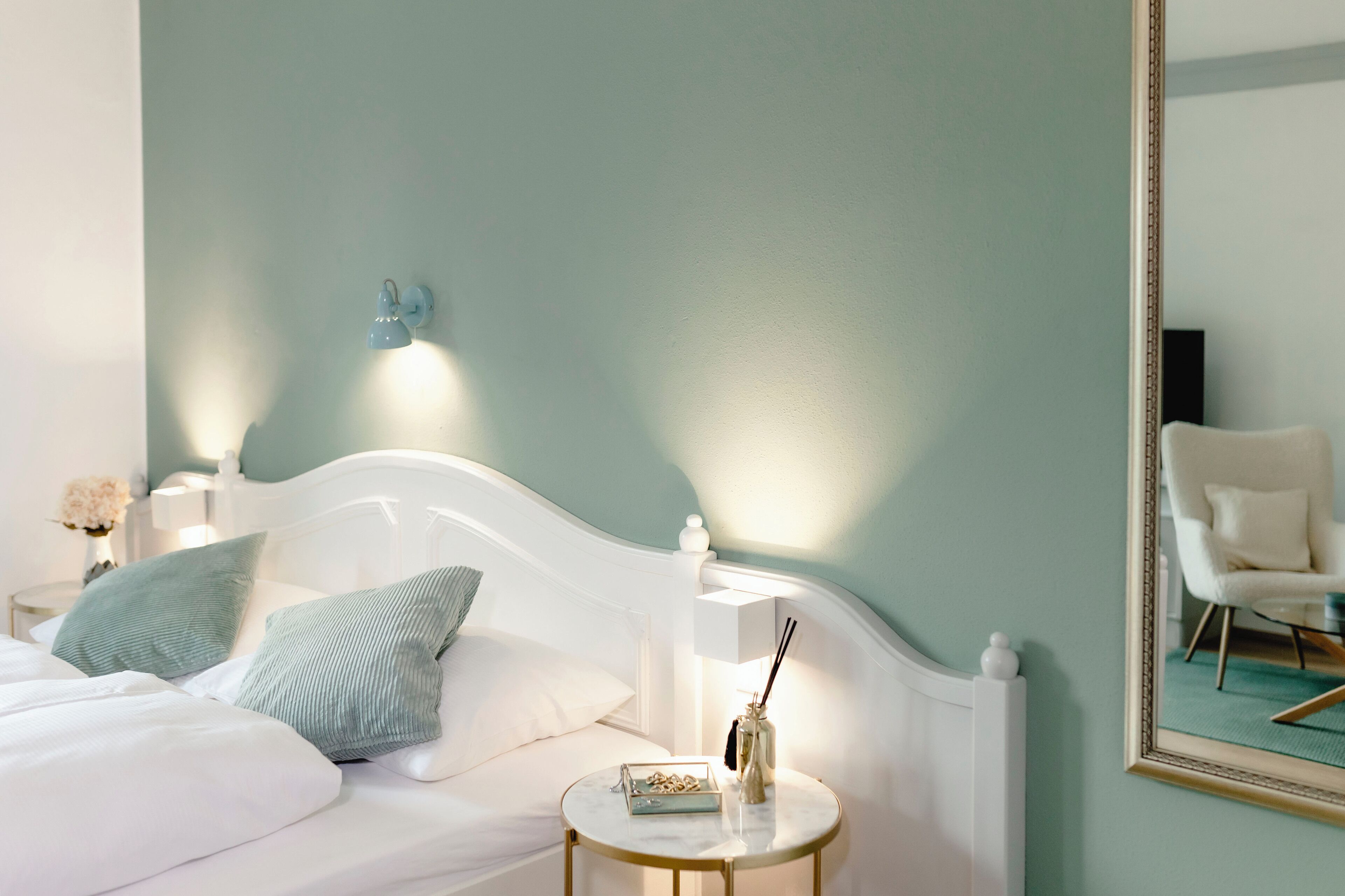 Quarto bem arrumado com cama, mesa de cabeceira, luminária e espelho na parede.