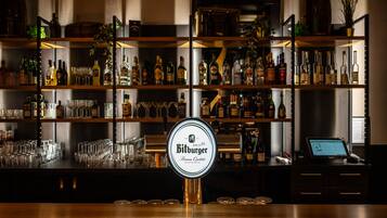 Uma área de bar com uma torneira de cerveja Bitburger, prateleiras com diversas garrafas de bebidas alcoólicas e um monitor de computador em um balcão.