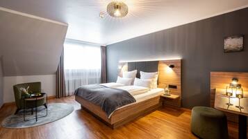 Quarto de hotel moderno com uma cama grande, escrivaninha, cadeira e vista para o exterior.
