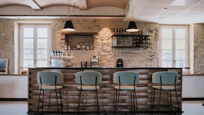 Uma área de bar com três bancos altos, uma parede de pedra e uma prateleira com garrafas e copos.