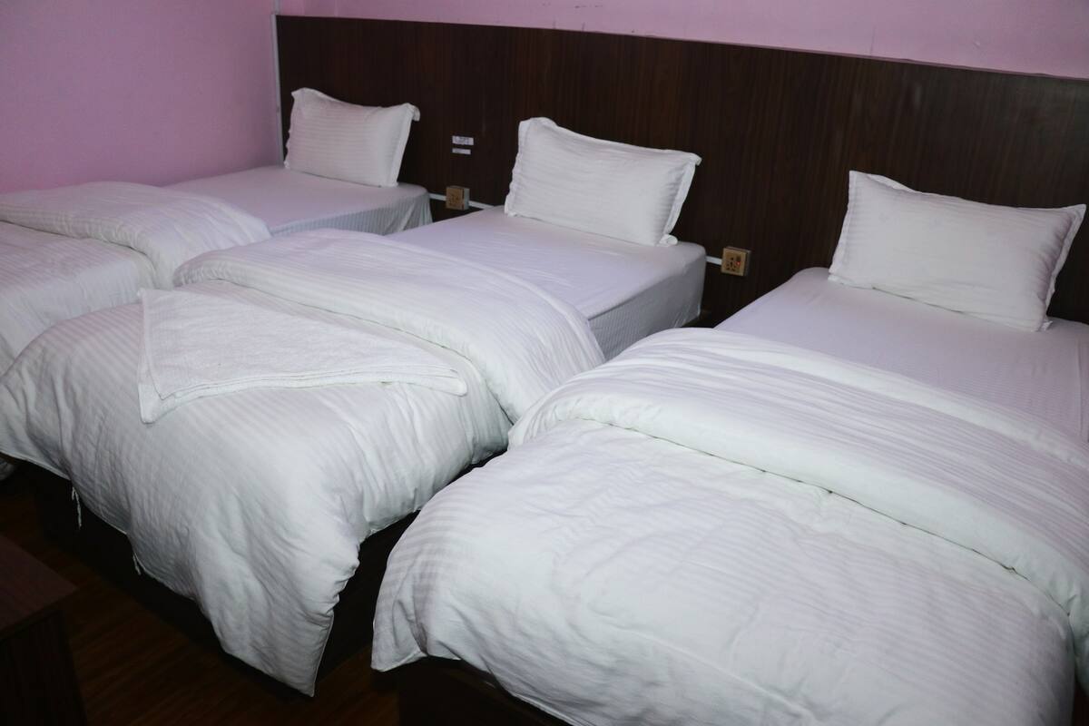 Quarto de hotel com três camas de solteiro, cada uma com roupa de cama branca e cabeceiras de madeira.