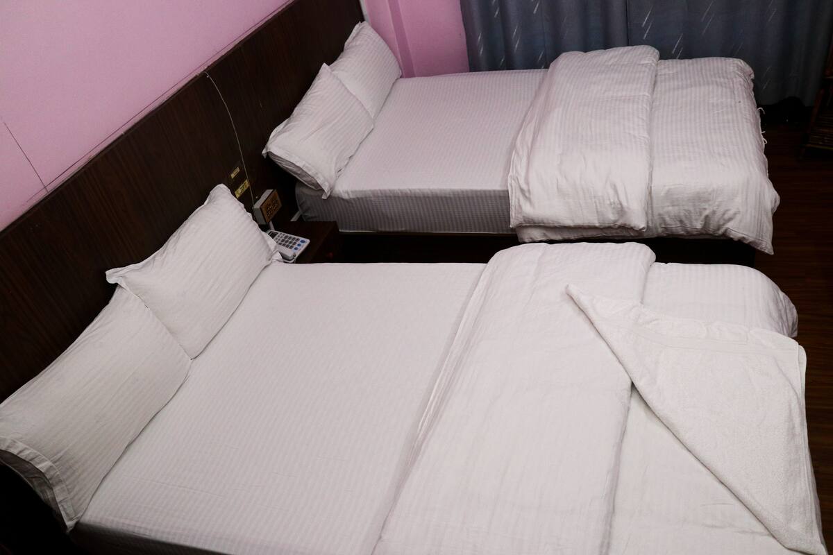 Quarto de hotel com duas camas de solteiro, cada uma com roupa de cama e almofadas brancas.