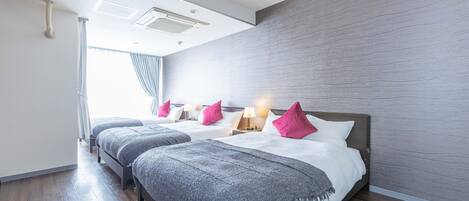 Quarto de hotel moderno com duas camas, uma janela grande com cortinas e piso de madeira.