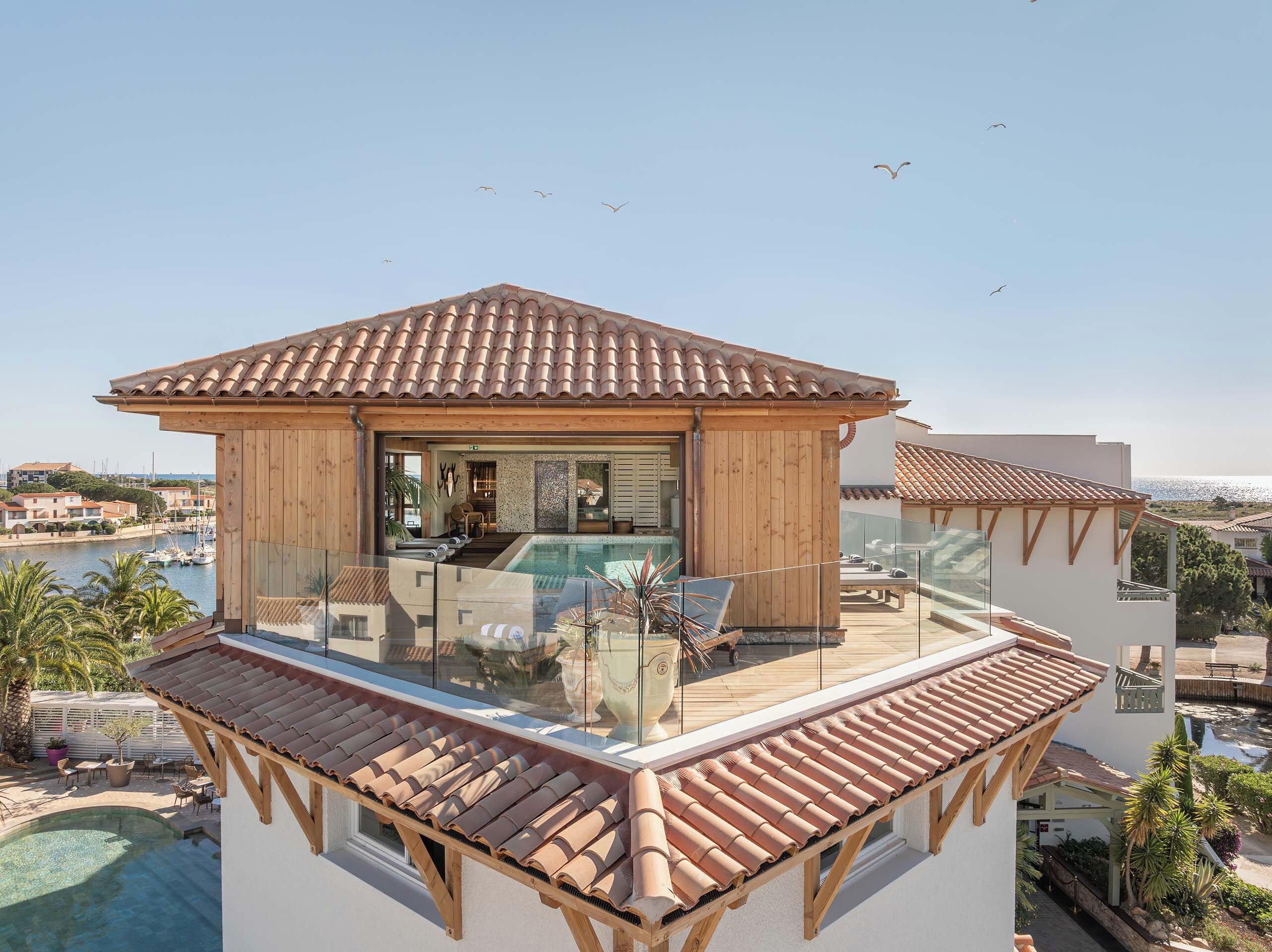 Uma área de piscina no terraço com pérgula de madeira, guarda-corpo de vidro e vista para o mar.