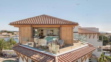 Uma área de piscina no terraço com pérgula de madeira, guarda-corpo de vidro e vista para o mar.
