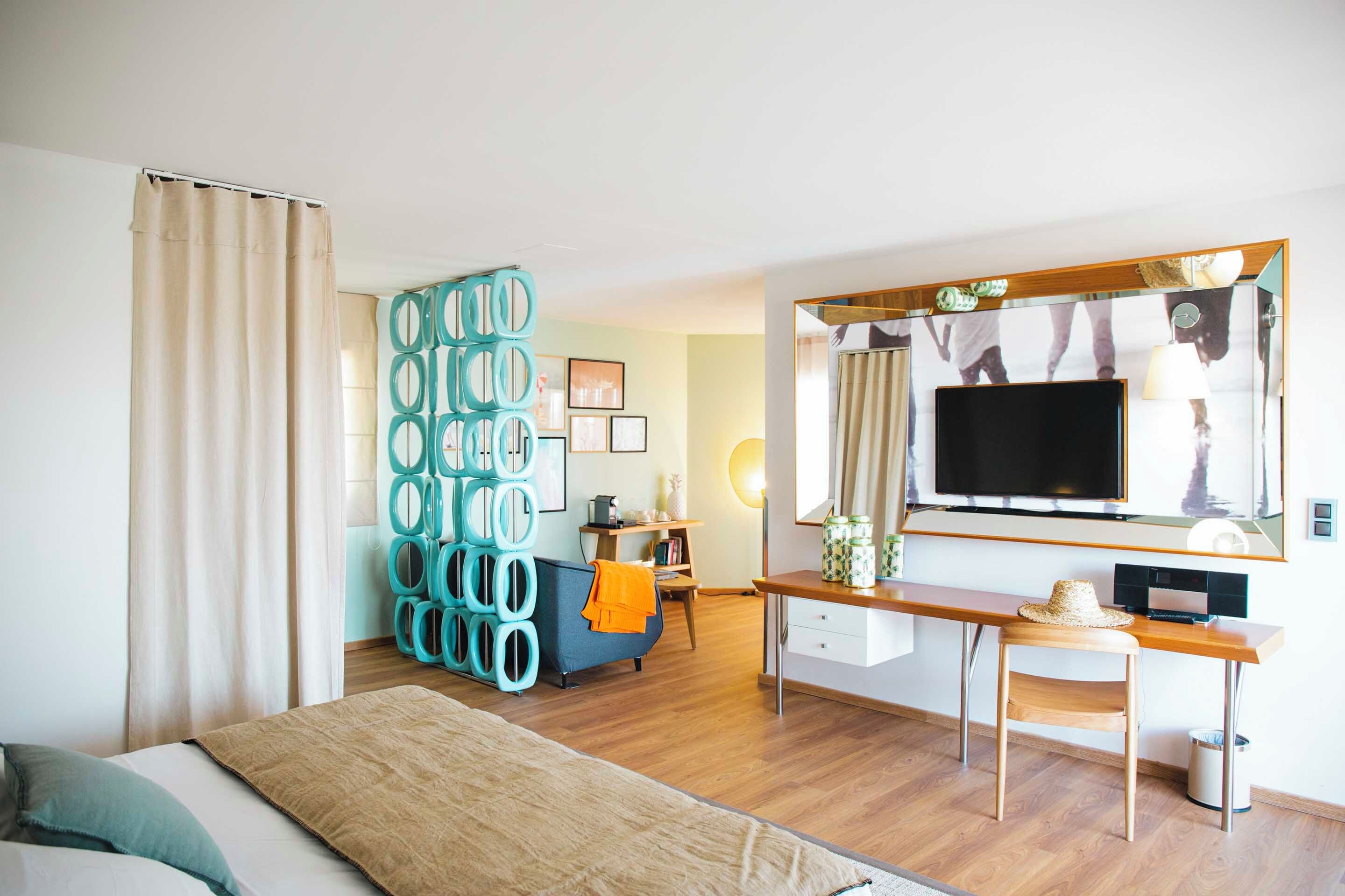 Quarto de hotel moderno com cama, escrivaninha, cadeira e uma televisão grande.