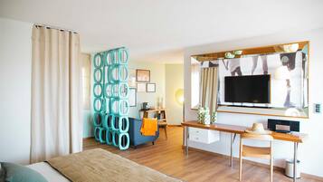 Quarto de hotel moderno com cama, escrivaninha, cadeira e uma televisão grande.