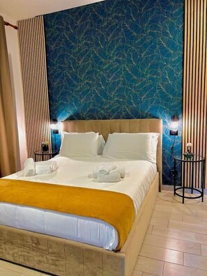 Quarto de hotel com cama, cabeceira, duas mesas de cabeceira e parede com padrão de folhagem.