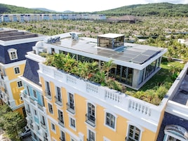 Um edifício com várias andares, varandas, painéis solares e um jardim no terraço.