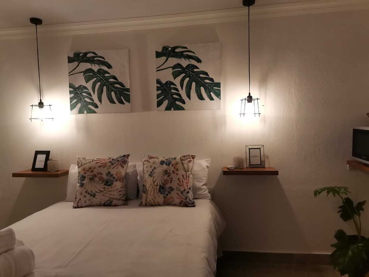 Quarto com cama, duas luminárias fixadas na parede e uma televisão sobre uma prateleira.